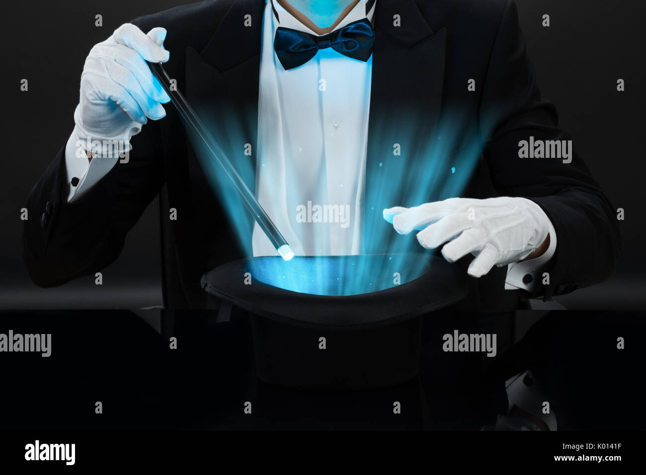 Midsection of magician holding magic wand over illuminated hat against ...