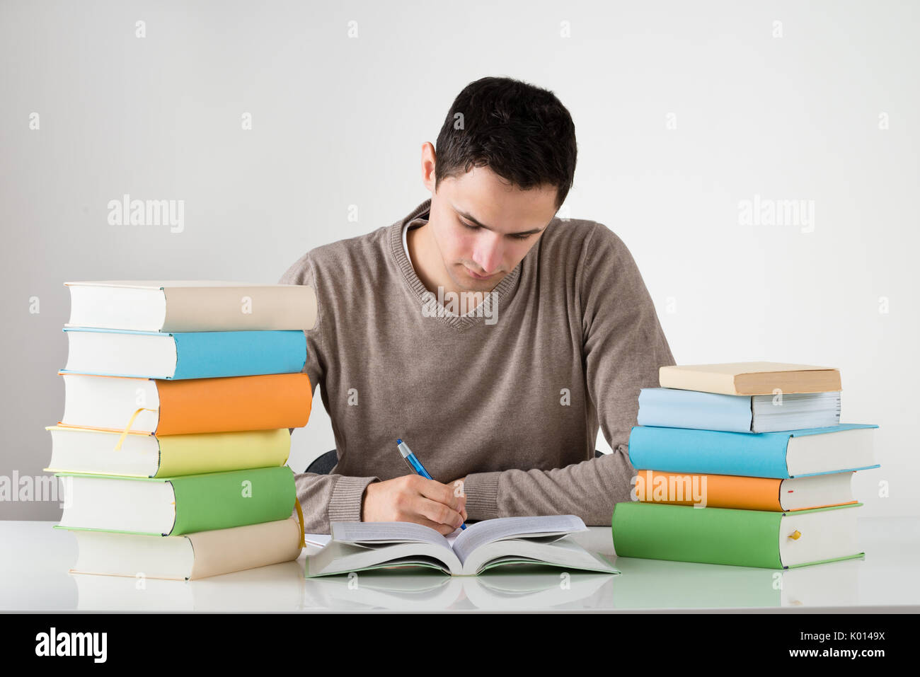 Young man writing in book while studying at table against white ...