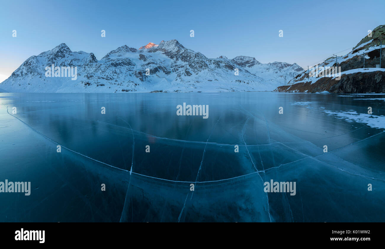 Panorama of frozen Lago Bianco surrounded by snowy peaks at dusk ...