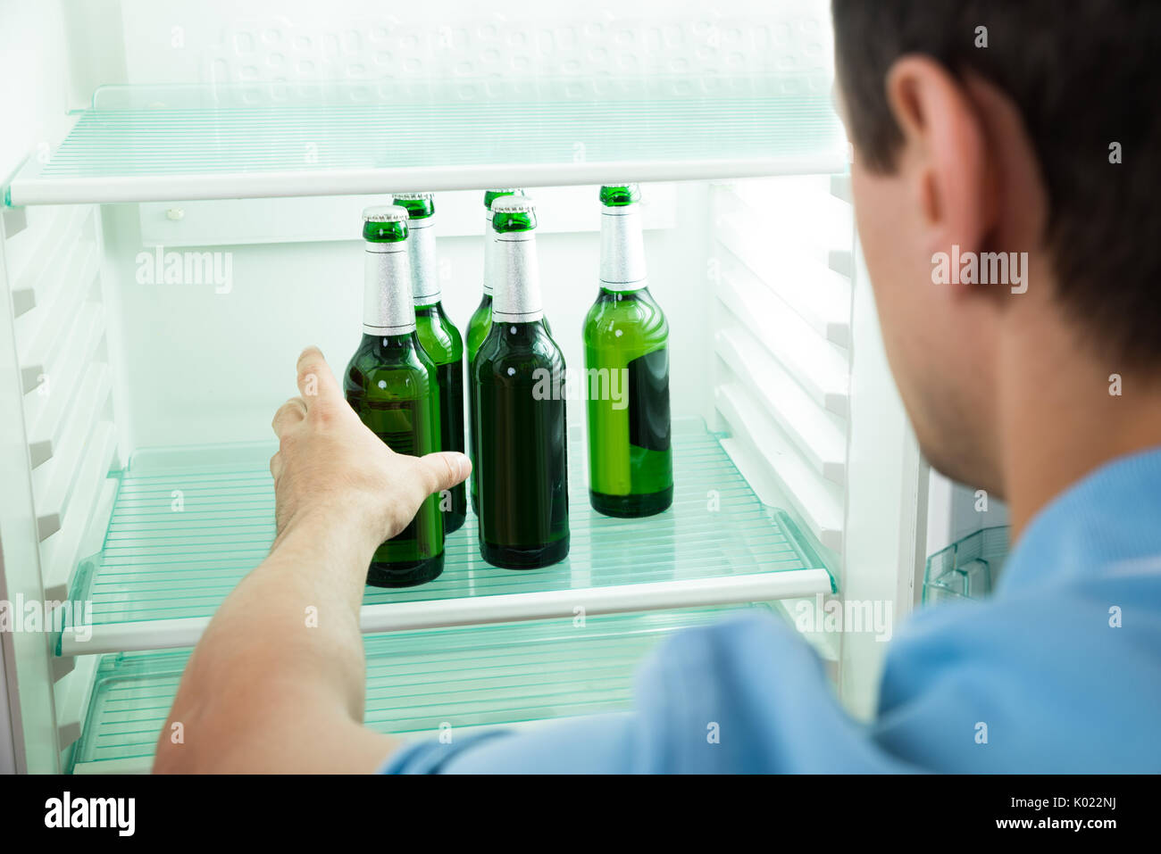 Side view of young man removing beer bottle from refrigerator at home ...
