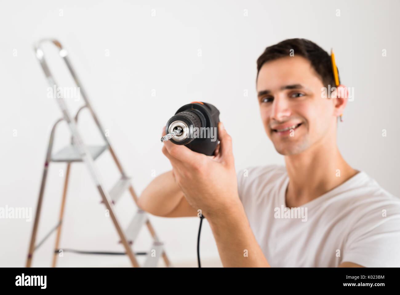 Portrait of smiling young man holding power drill against white wall at ...