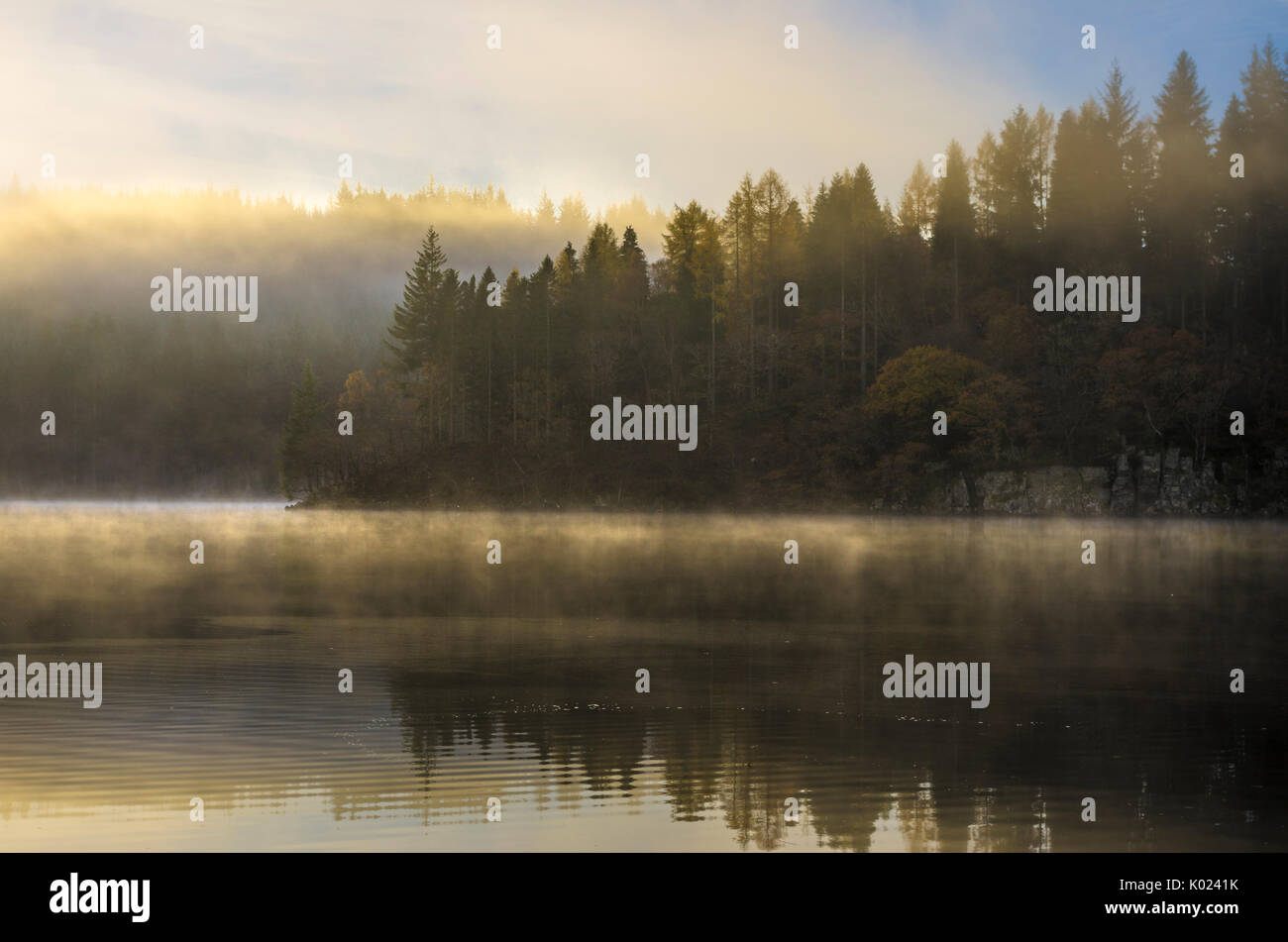 Sunlight breaking through the mist on light up trees reflection, Loch ...