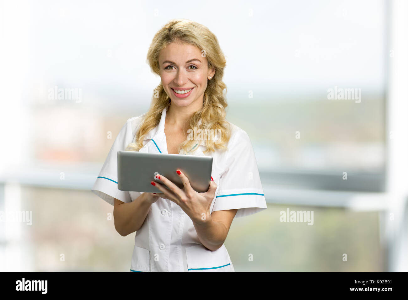Joyful young nurse with computer tablet. Smiling young girl in white ...