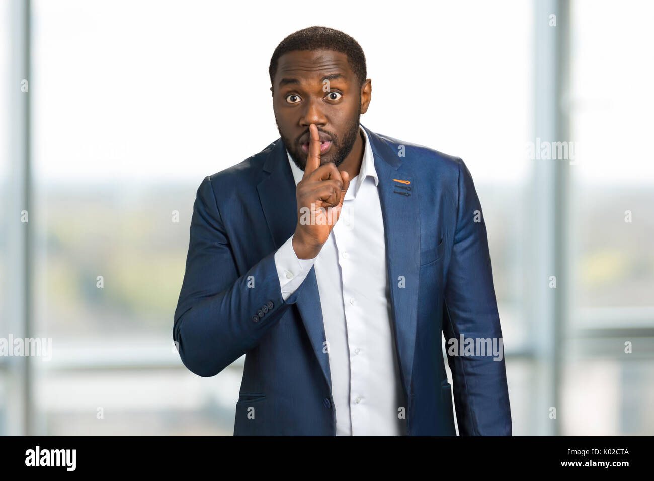 Businessman holding index finger on lips. Black man showing silence ...