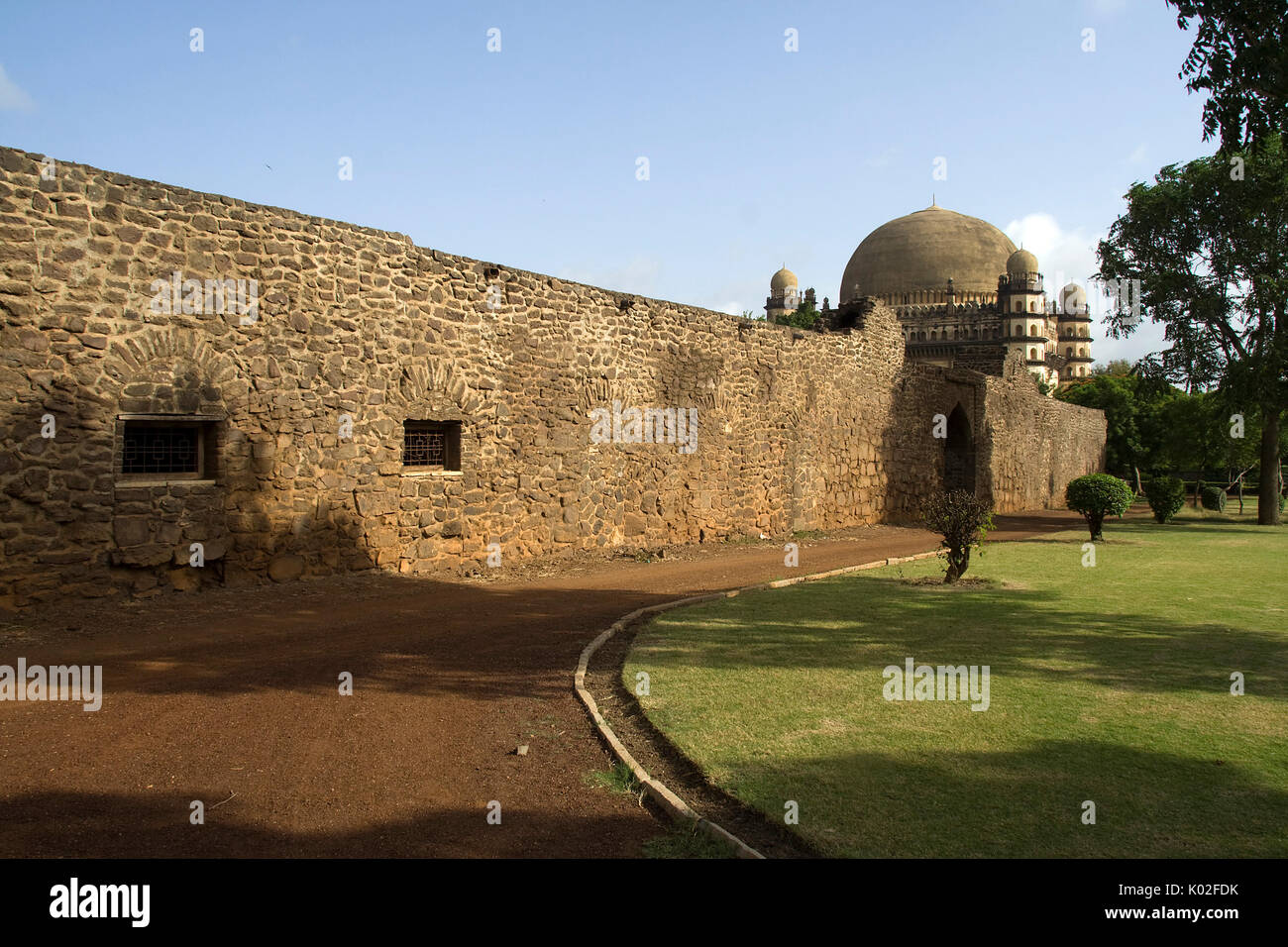 Lengthy stone wall partially hides the mammoth monument Gol Gumbaz in ...
