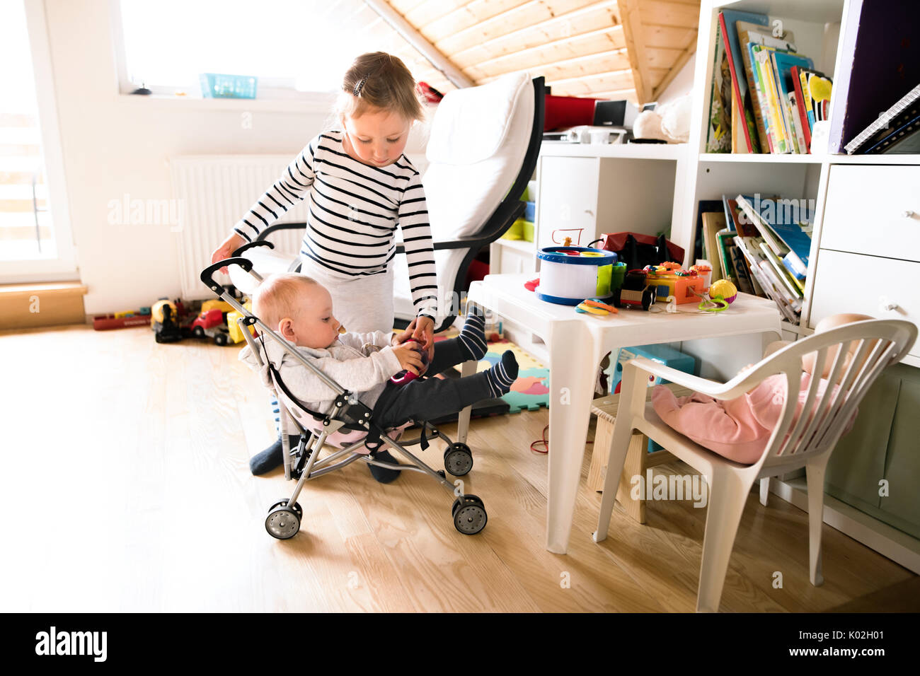 Little girl at home with baby brother in toy stroller Stock Photo - Alamy