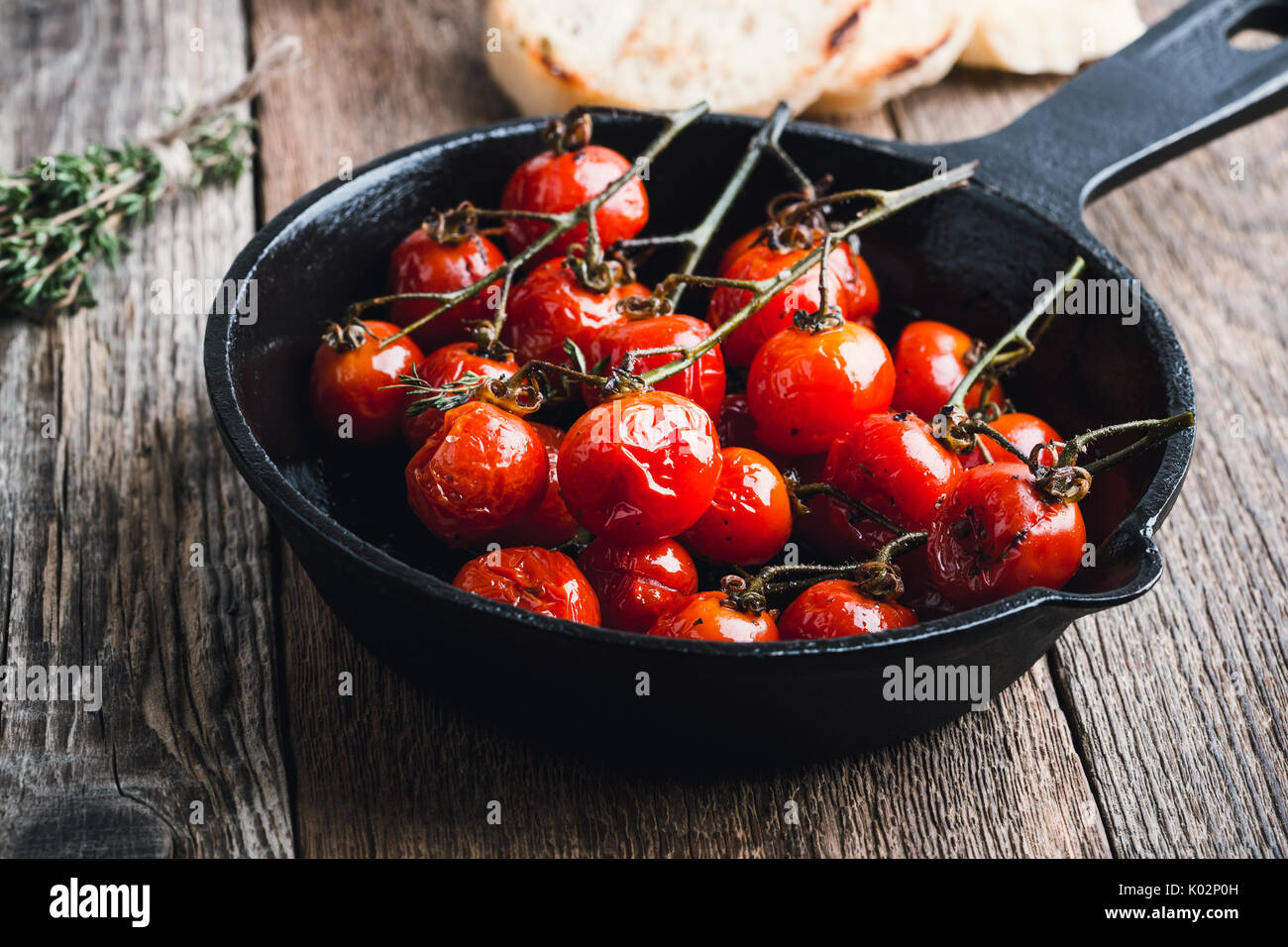 Roasted cherry tomatoes in cast iron skillet on rustic wooden board ...