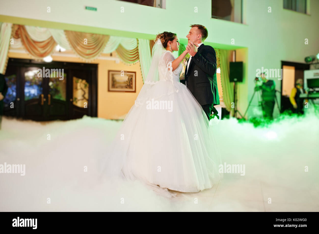 Beautiful wedding couple dancing their first dance in the huge hall with heavy smoke, different ...