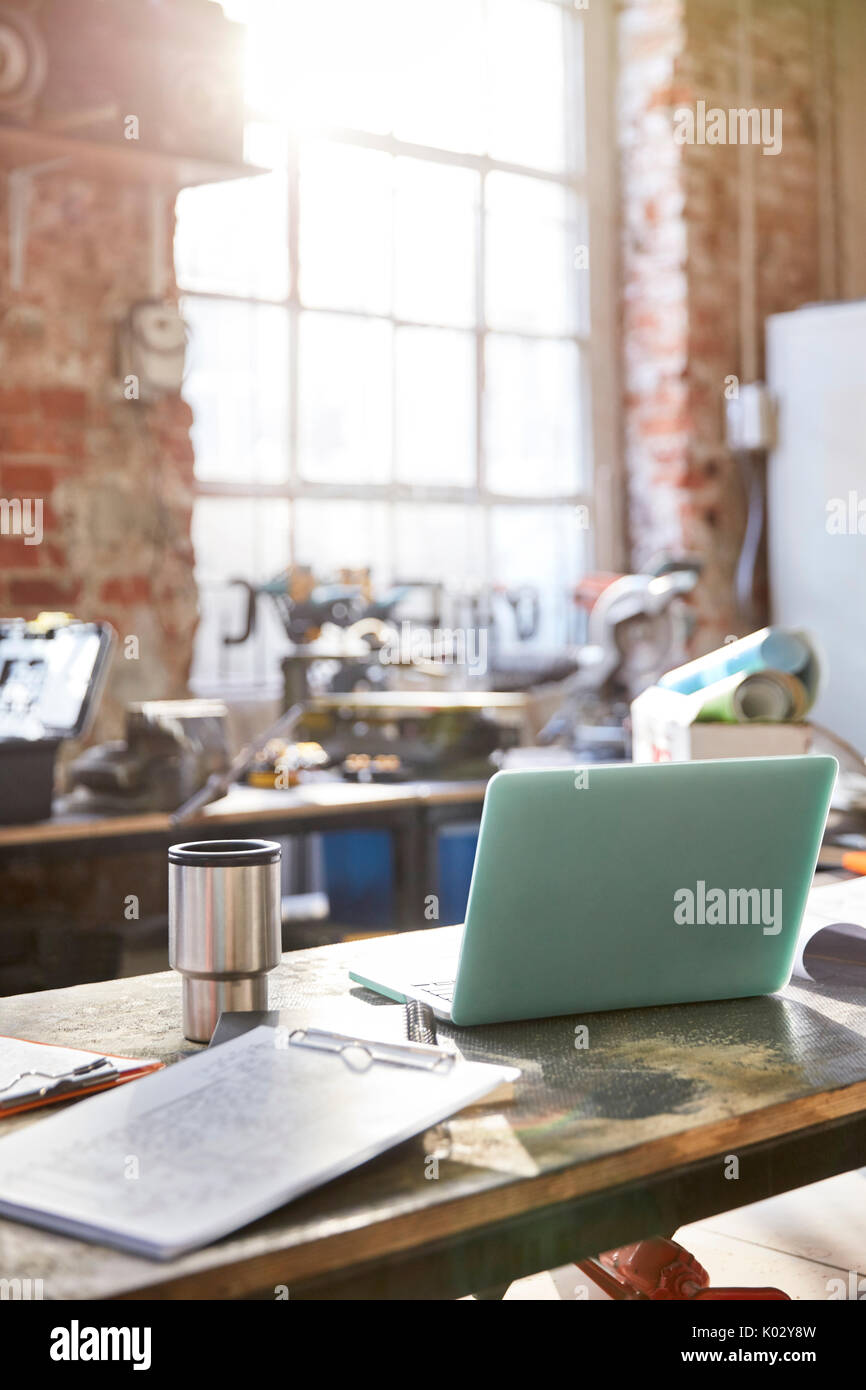 Laptop, coffee and clipboard on workbench in workshop Stock Photo - Alamy