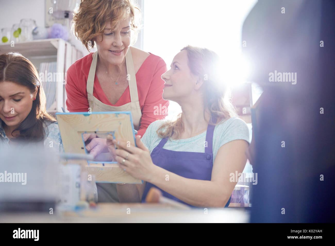 Female instructor helping student painting picture frame in art class ...