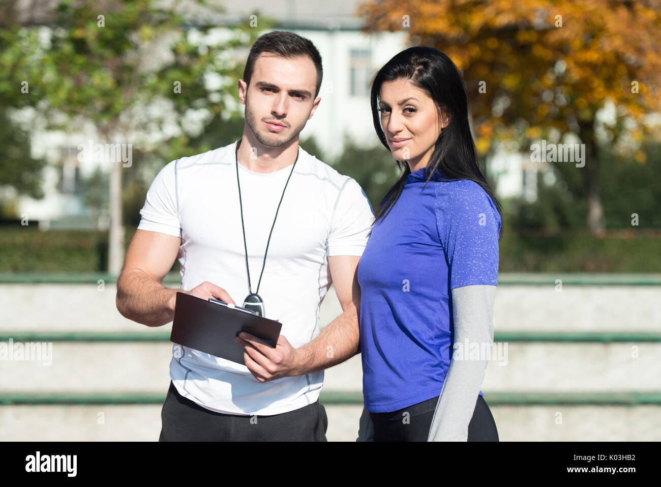 Personal Trainer Takes Notes While Young Woman Exercise in City Park ...