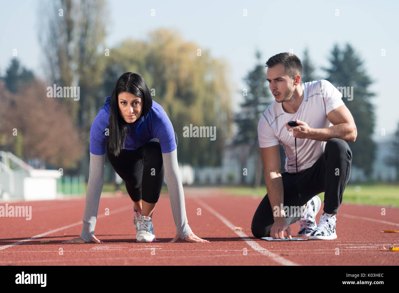 Athletic Personal Trainer Helping Female To Sprint on the Running Track ...