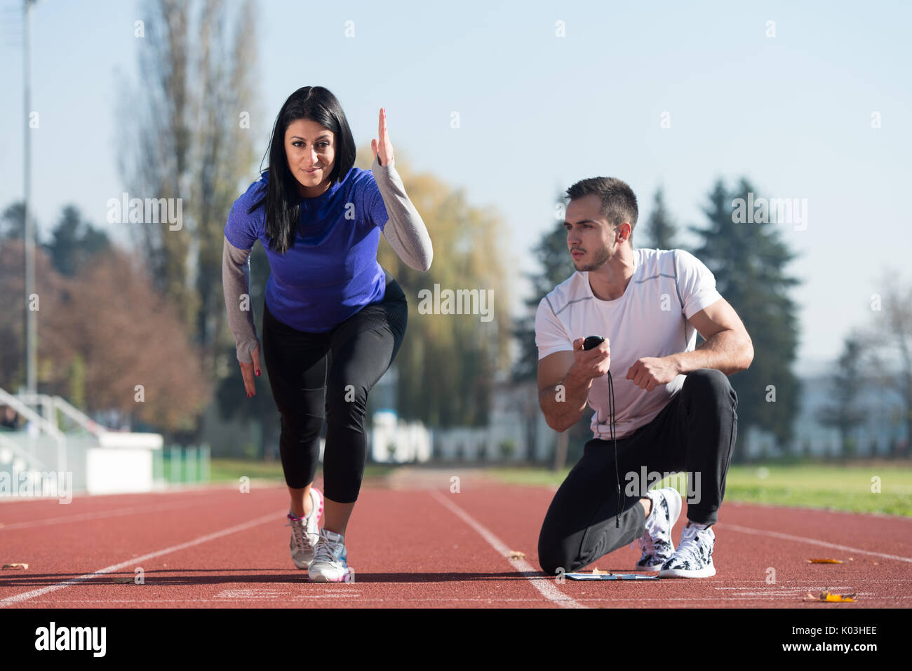 Athletic Personal Trainer Helping Female To Sprint on the Running Track ...