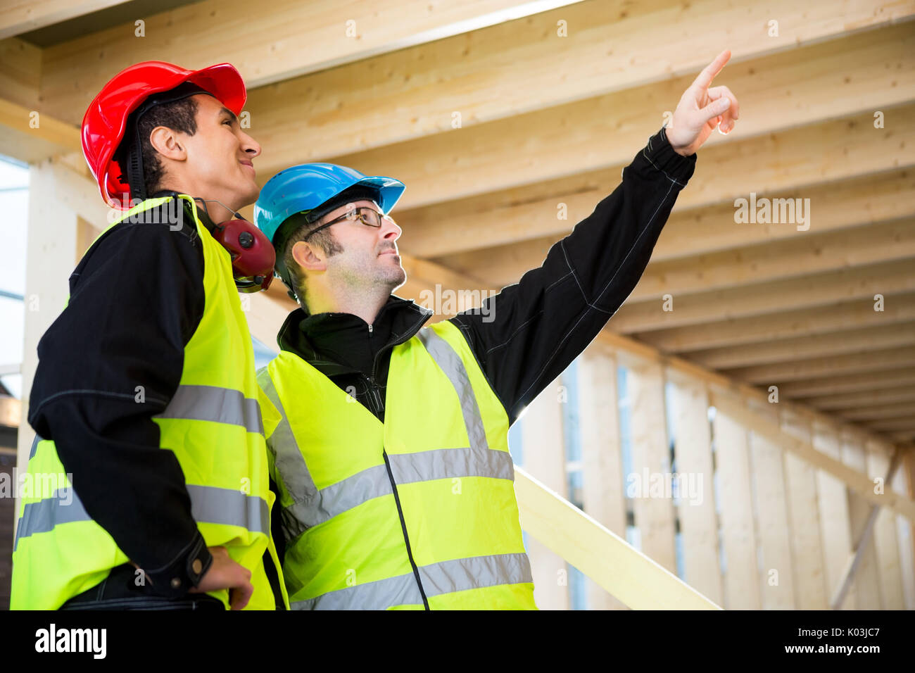 Carpenter Pointing Towards Roof While Standing By Colleague Stock Photo ...