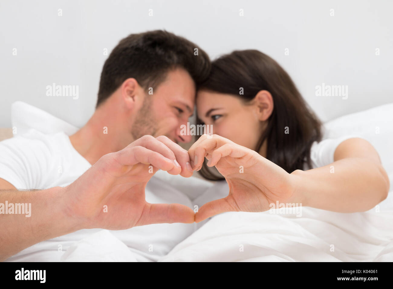 Couple Lying On Bed Forming Heart Shape With Hand Stock Photo - Alamy