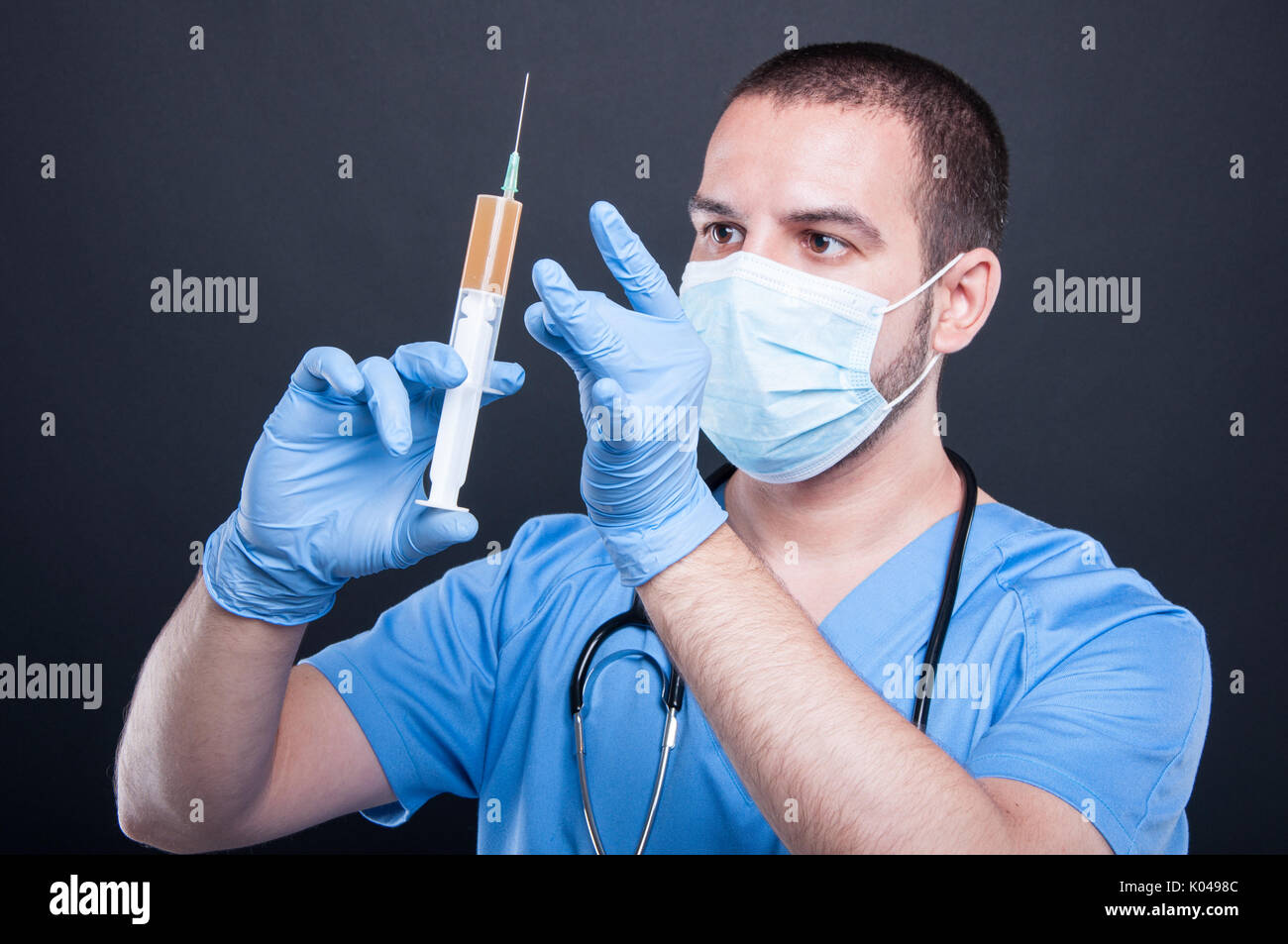 Plastic surgeon wearing scrubs checking and preparing syringe on black ...