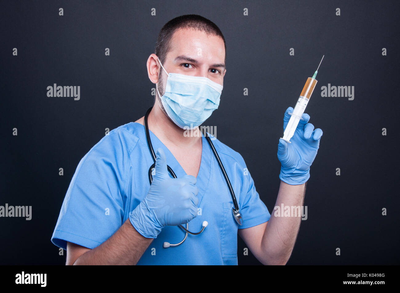 Medic wearing scrubs showing syringe and like gesture on black ...