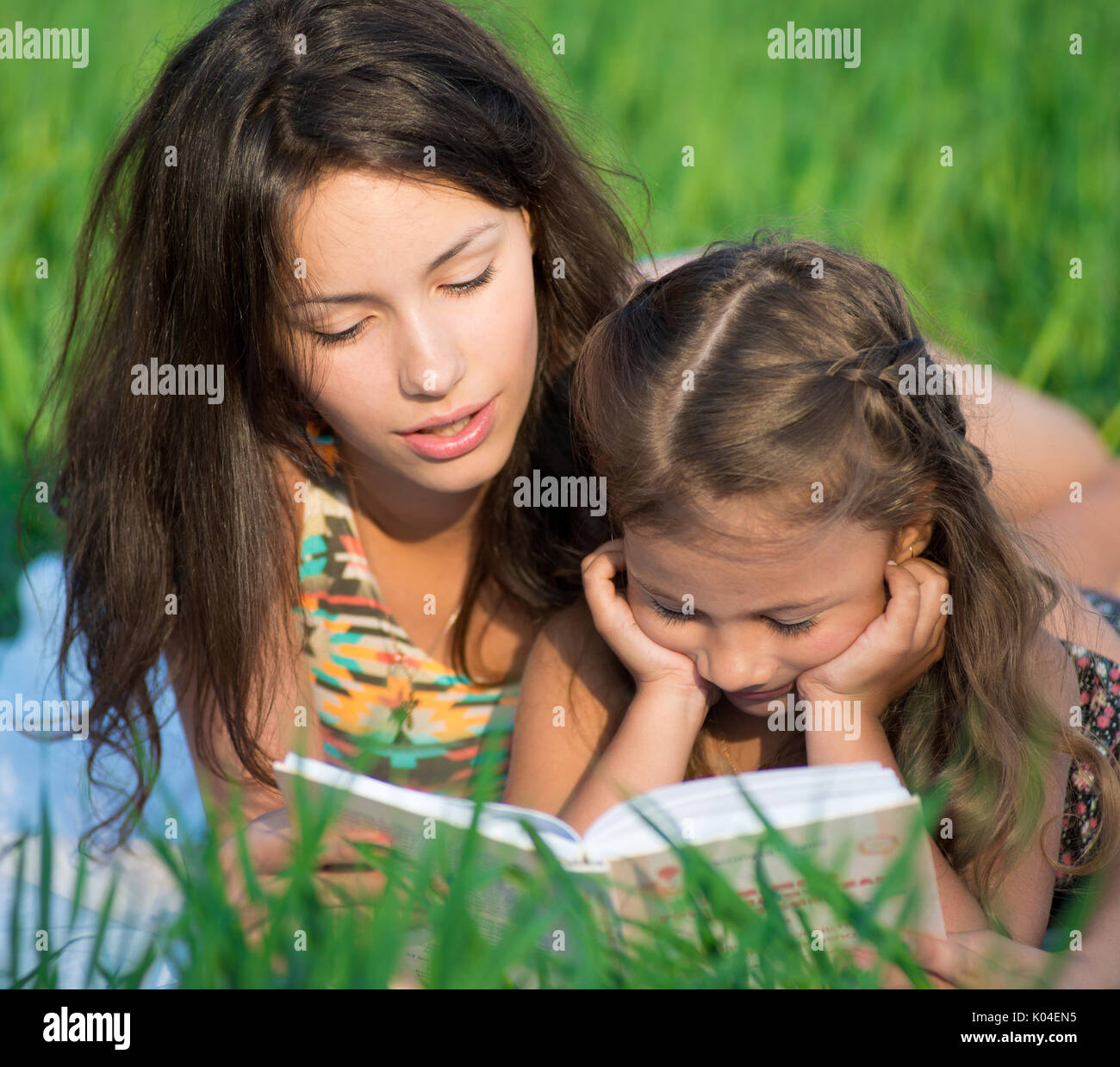 Happy girls reading book on green grass Stock Photo - Alamy