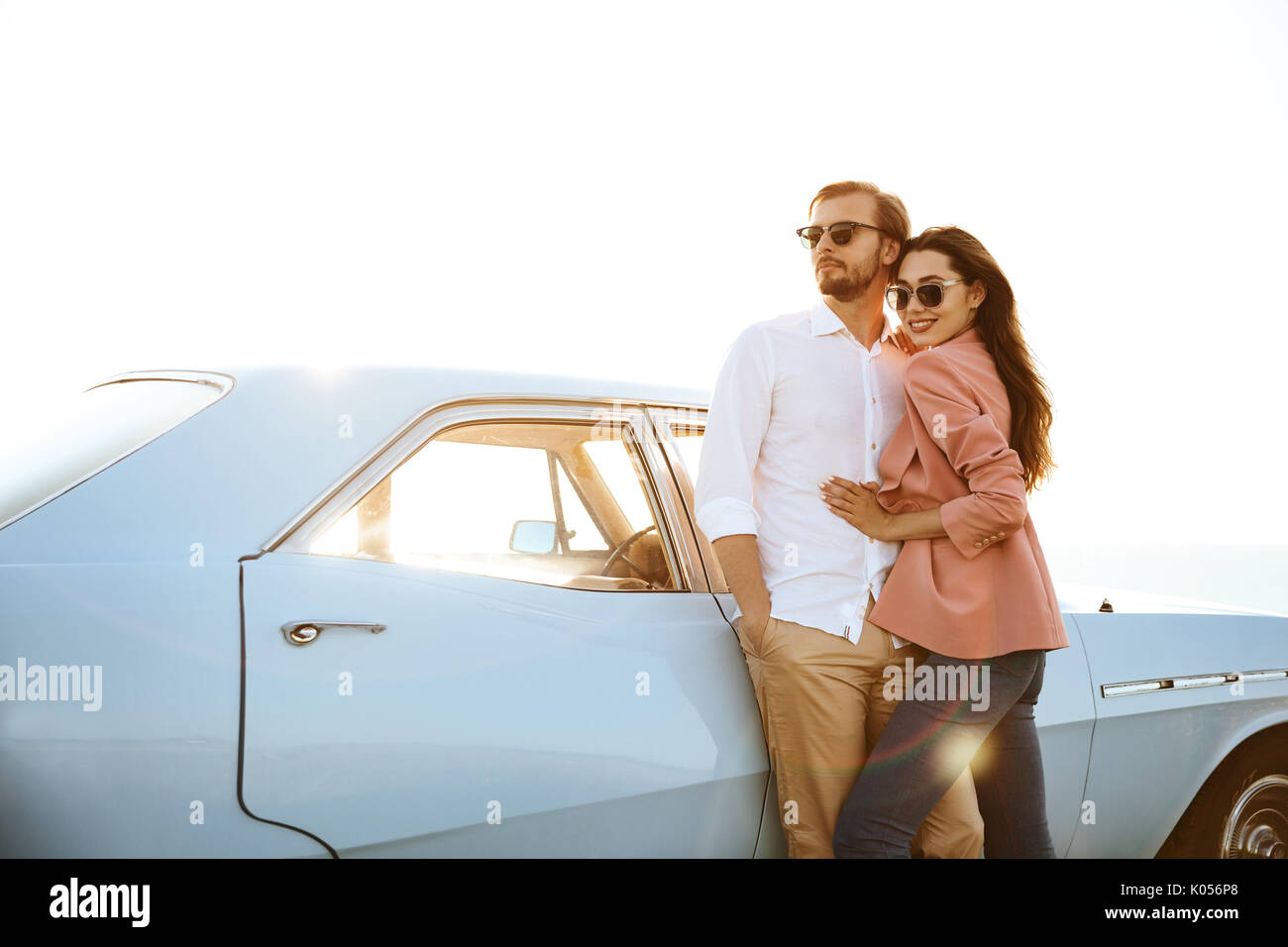 Happy young couple hugging while standing outside and leaning on a car ...