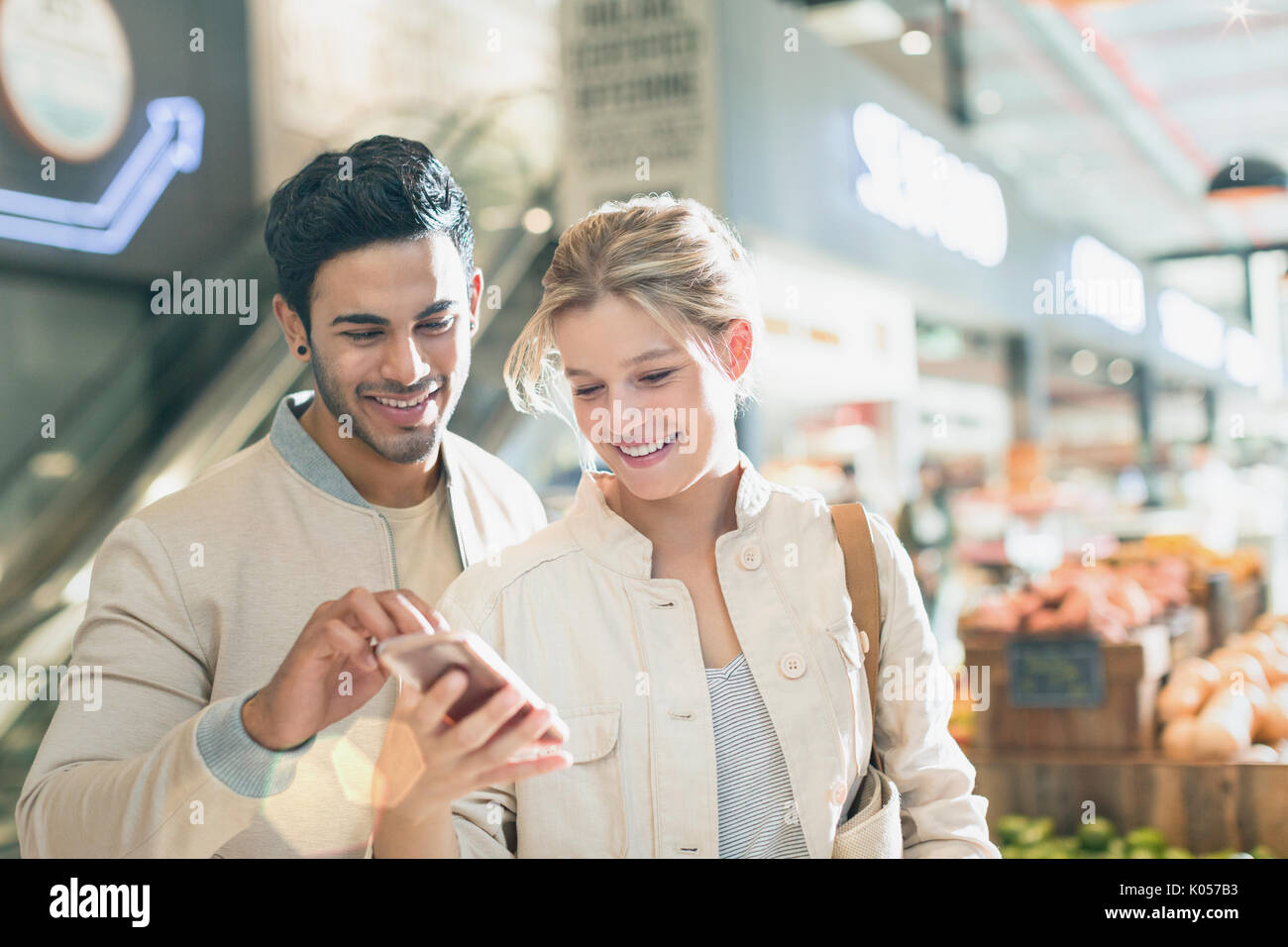 Smiling young couple using cell phone in grocery store market Stock ...