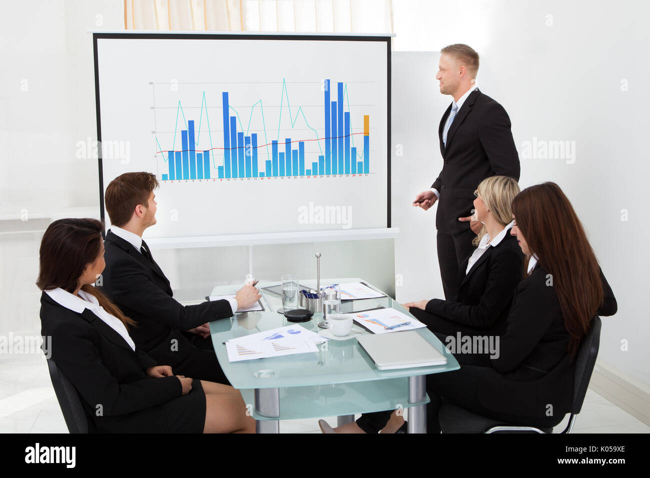 Businessman giving presentation on projector screen to colleagues in ...
