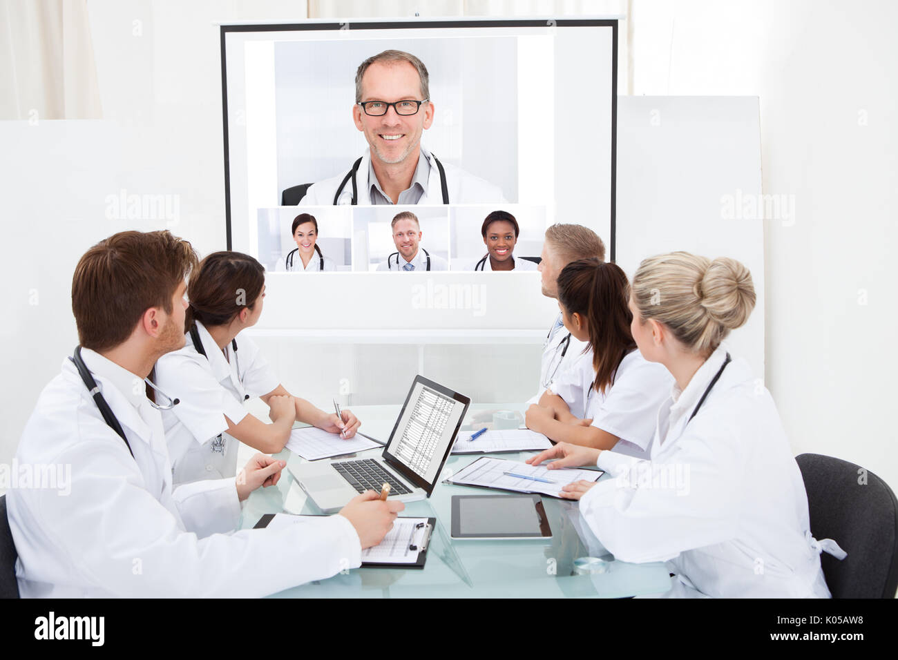 Team of doctors looking at projector screen in video conference meeting ...