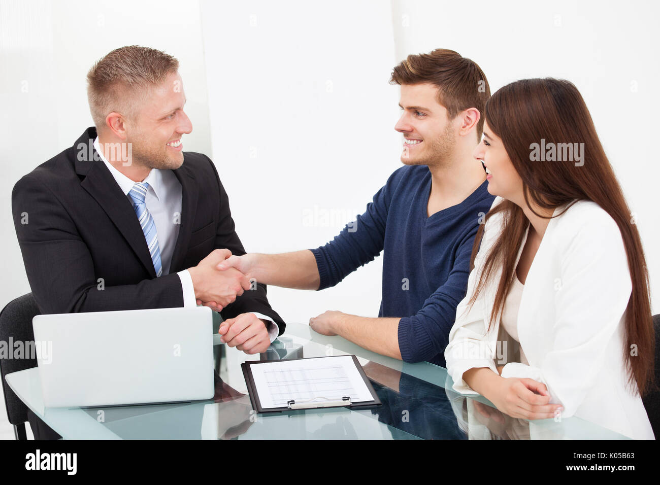 Smiling financial advisor shaking hand with couple at office desk Stock ...