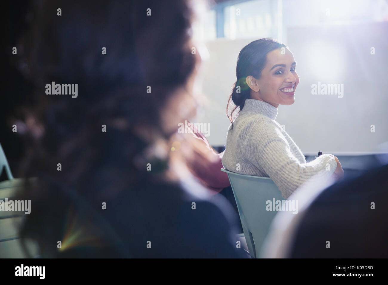 Smiling businesswoman turning, looking back in conference audience ...