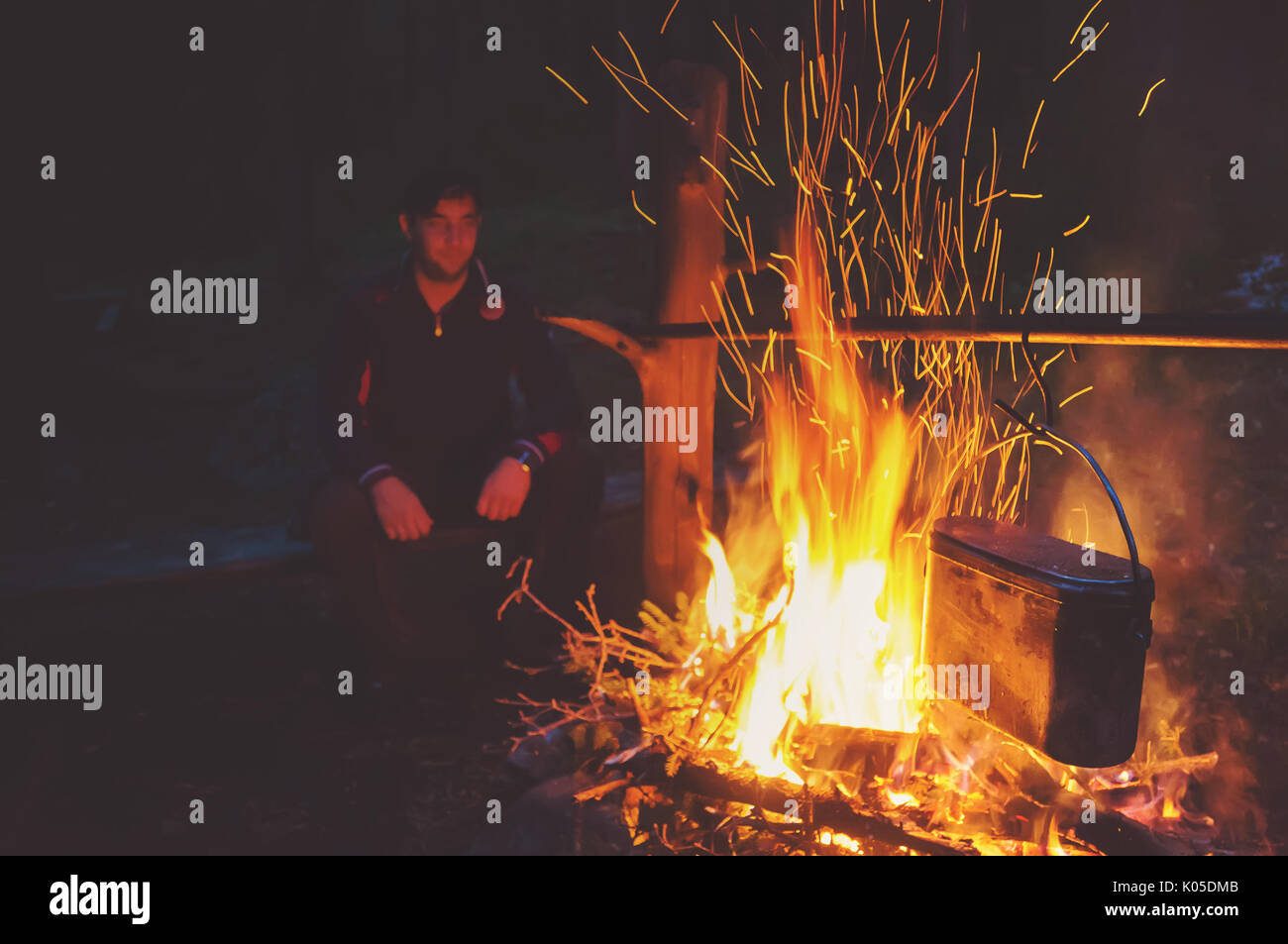 Hiking tourist have a rest in his camp at night near campfire. Guy ...