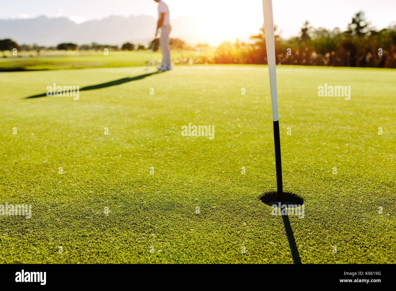 Golf hole and flag in the green field with golfer in background ...