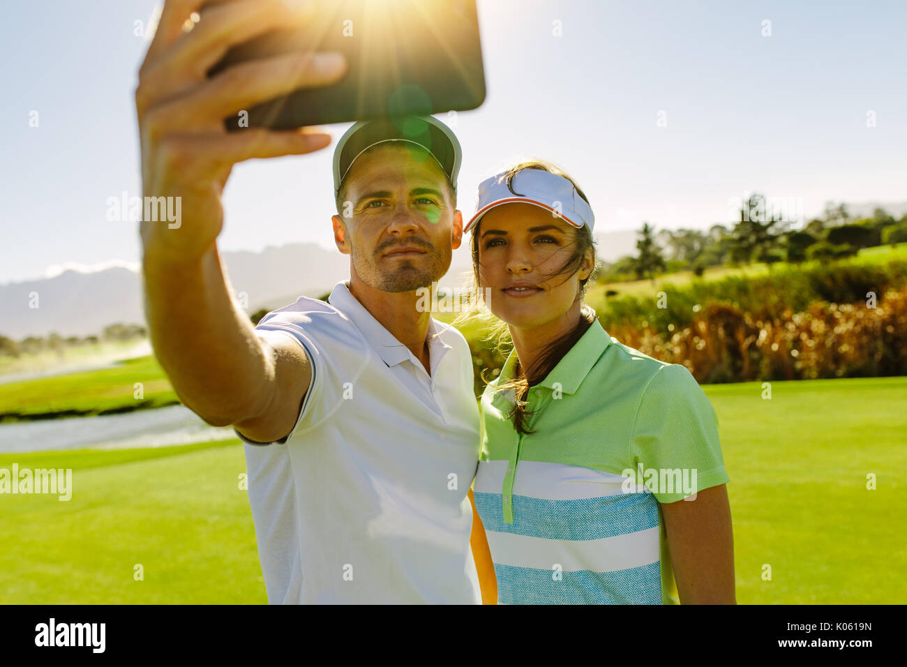 Male and female golfers taking selfie with mobile phone at golf course ...