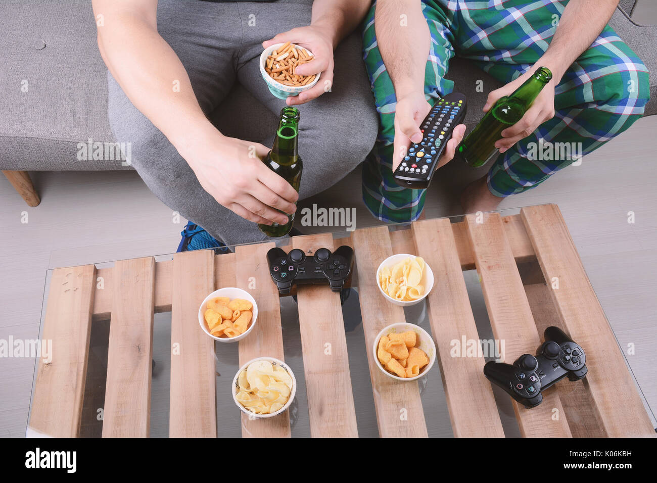 Portrait of two friends playing videogames, eating snacks and drinkng ...