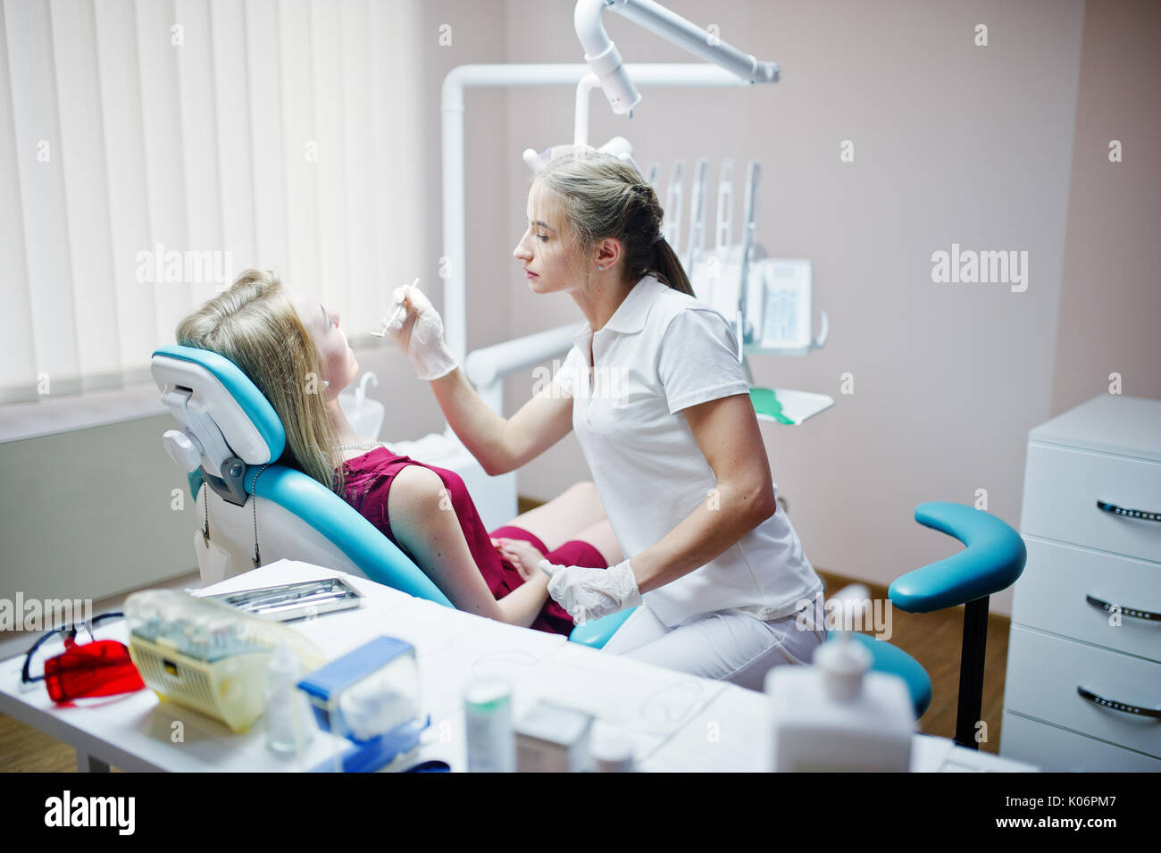 Attractive patient in red-violet dress laying on the dental chair while ...