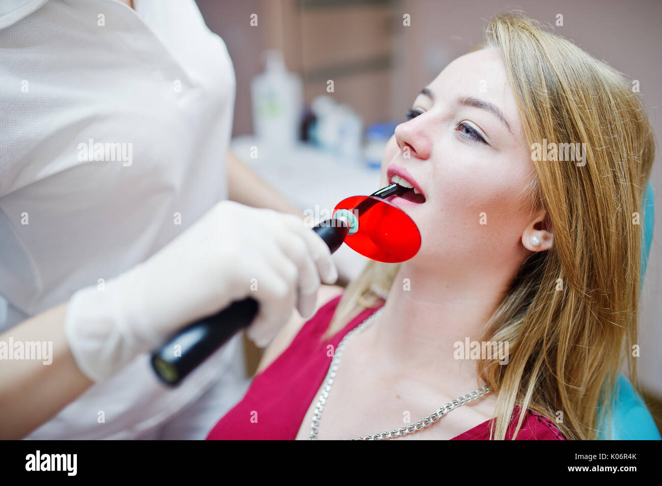 Attractive patient in red-violet dress laying on the dental chair while ...