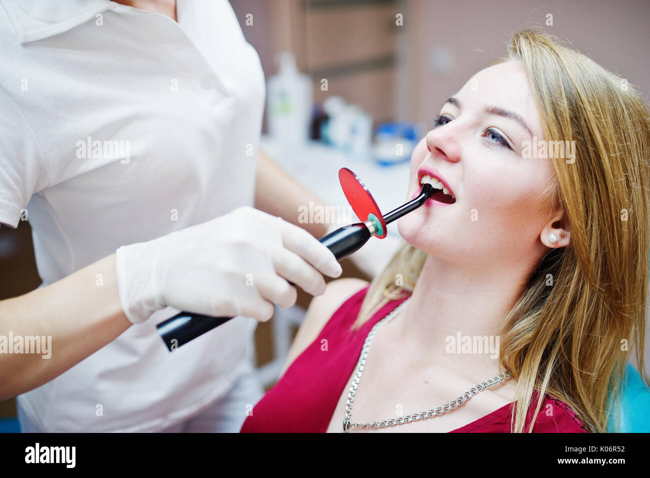 Attractive patient in red-violet dress laying on the dental chair while ...