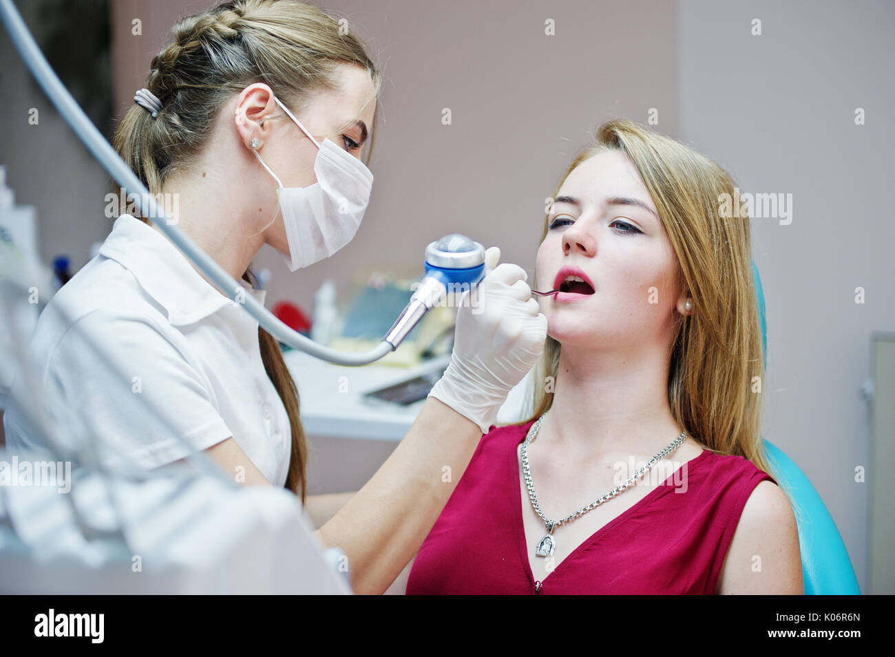 Attractive patient in red-violet dress laying on the dental chair while ...