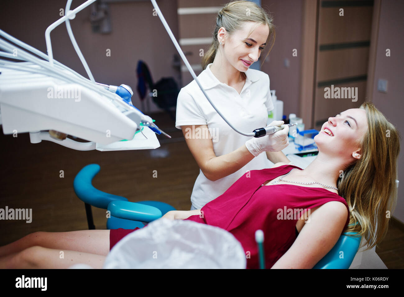 Attractive patient in red-violet dress laying on the dental chair while ...