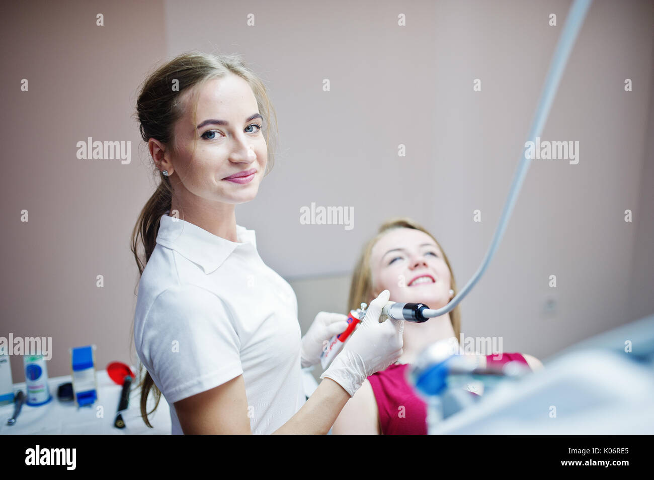 Attractive patient in red-violet dress laying on the dental chair while ...