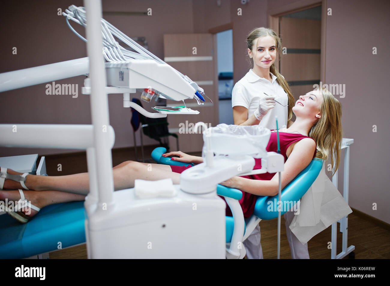Attractive patient in red-violet dress laying on the dental chair while ...