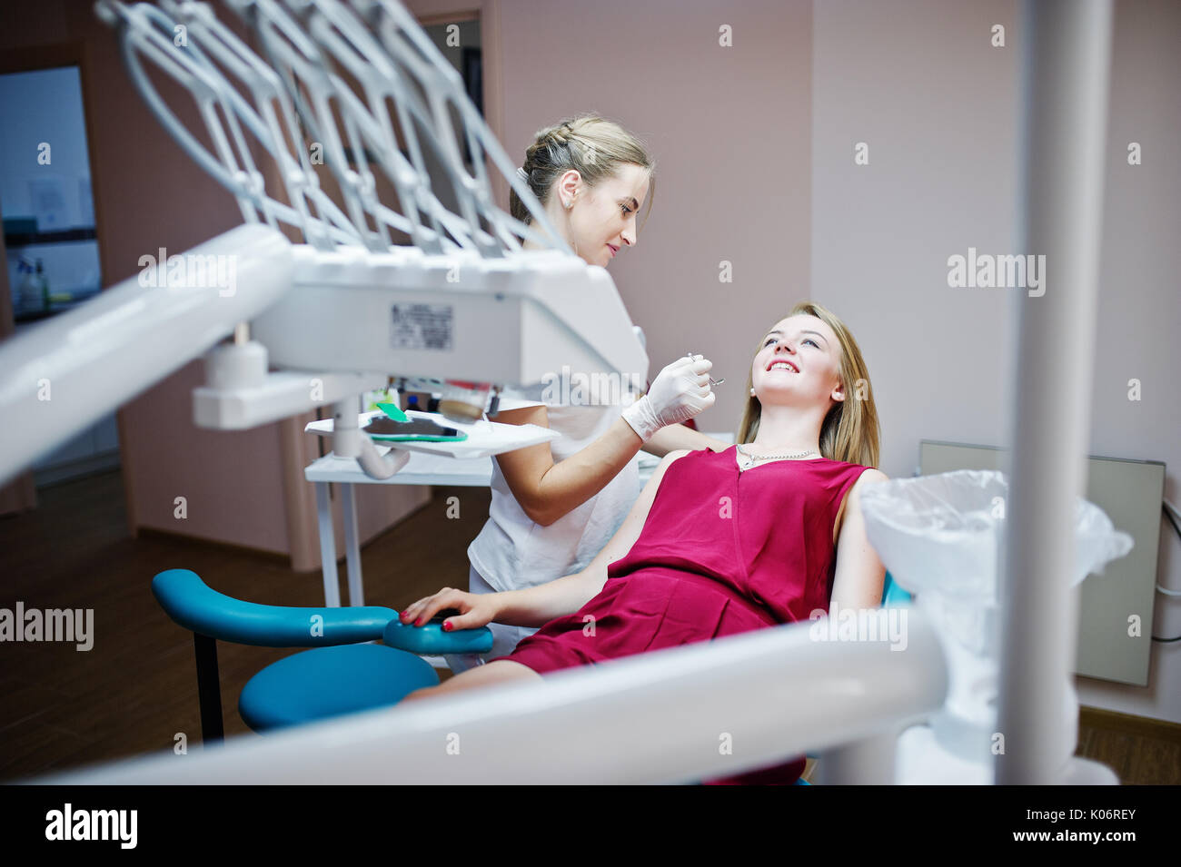 Attractive patient in red-violet dress laying on the dental chair while ...