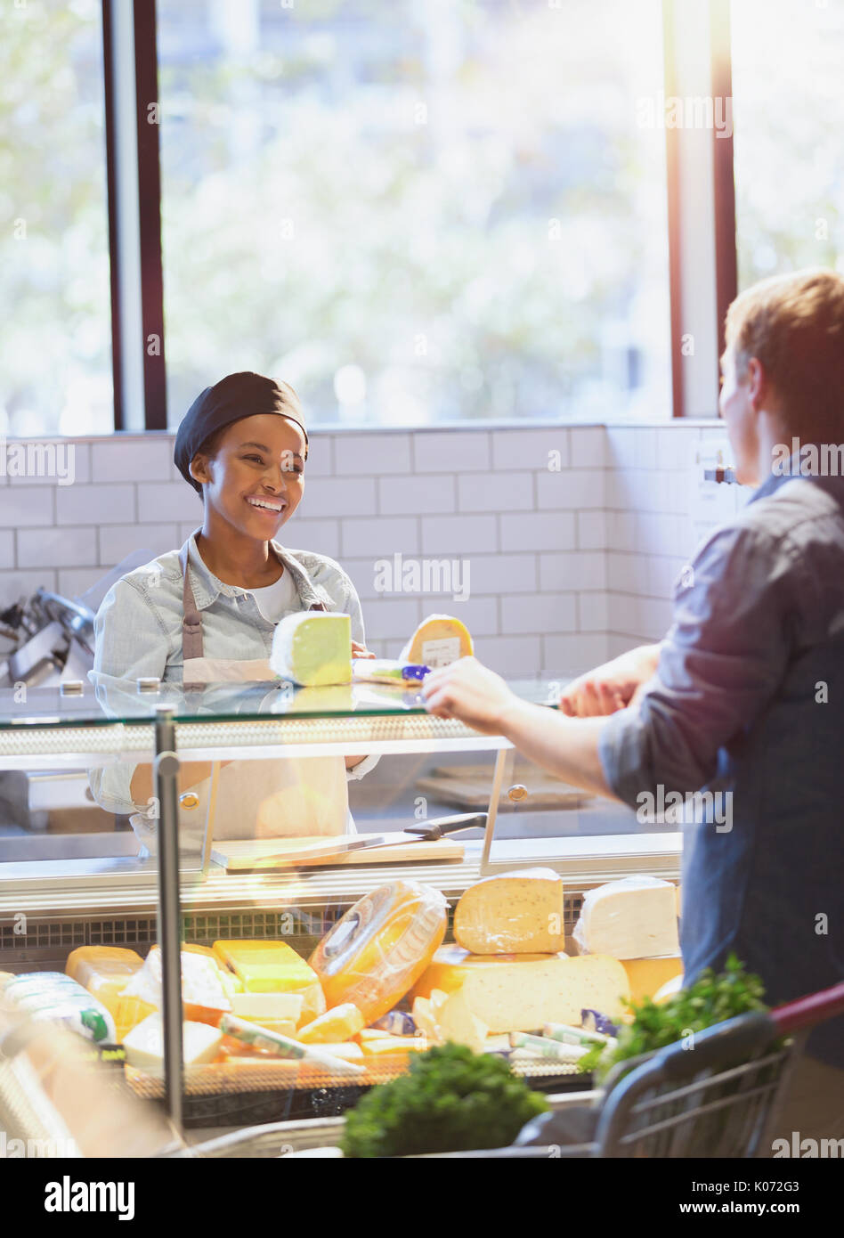Smiling young woman helping customer at cheese counter in grocery store ...