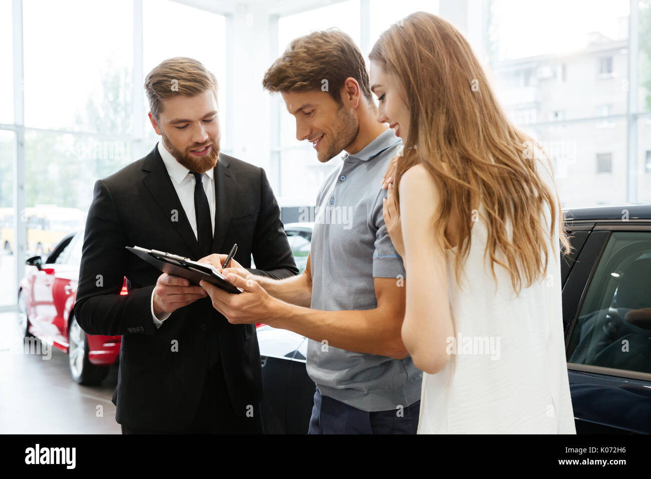 Handsome salesman filing documents with his happy clients at the ...