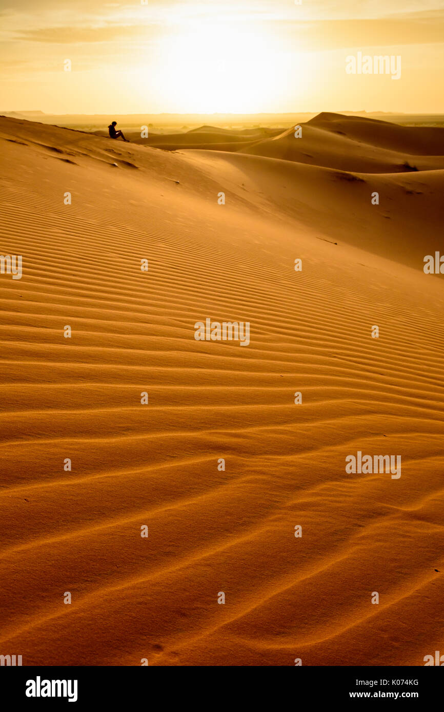 Sand lines at Erg Chebbi sand dune at sunrise. A woman is sitting on a ...