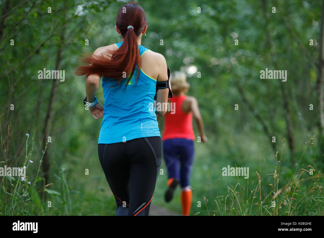Photo from back of two female athletes running in forest at summer ...