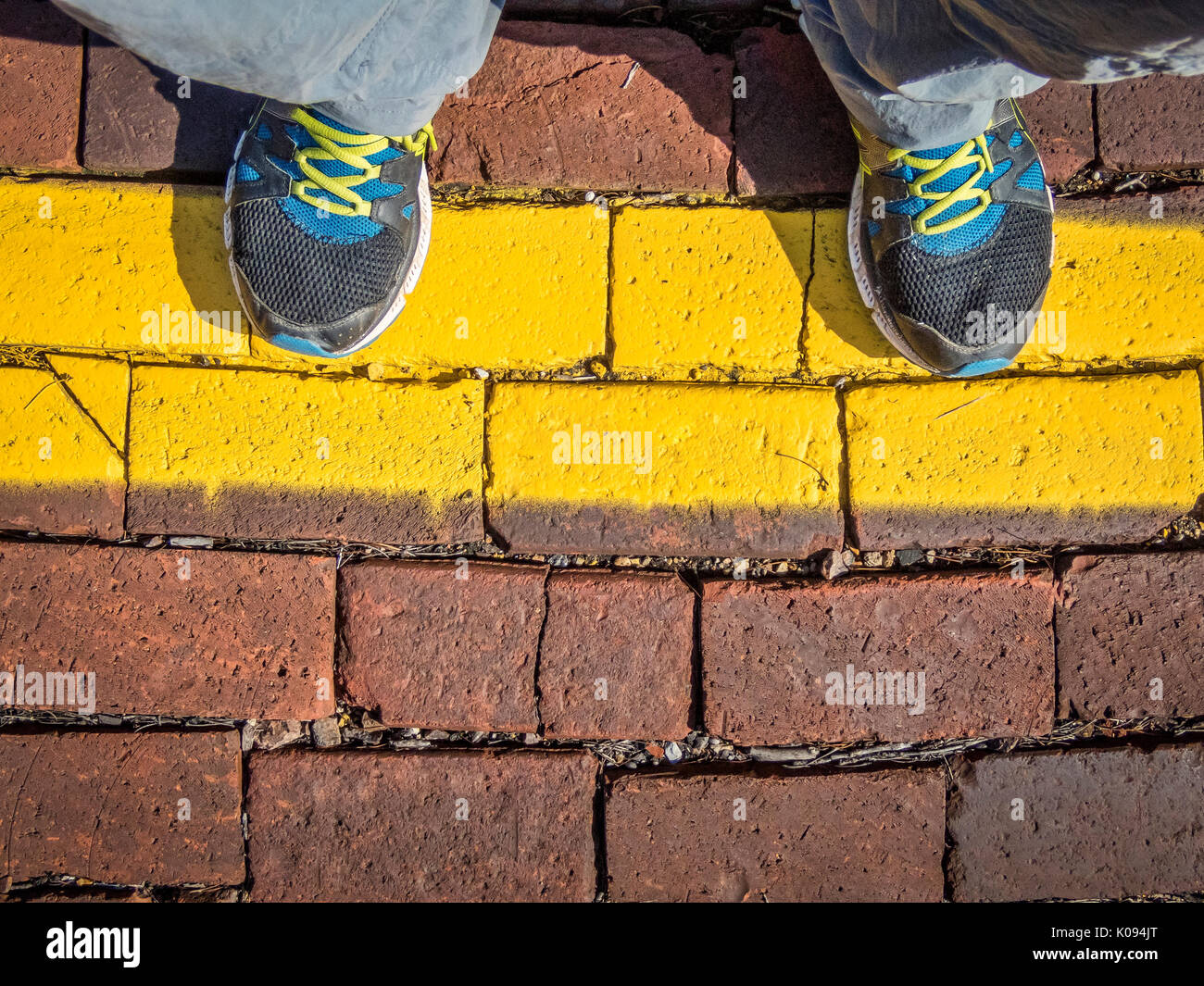 Waiting behind a yellow line - man's feet on a train station platform ...