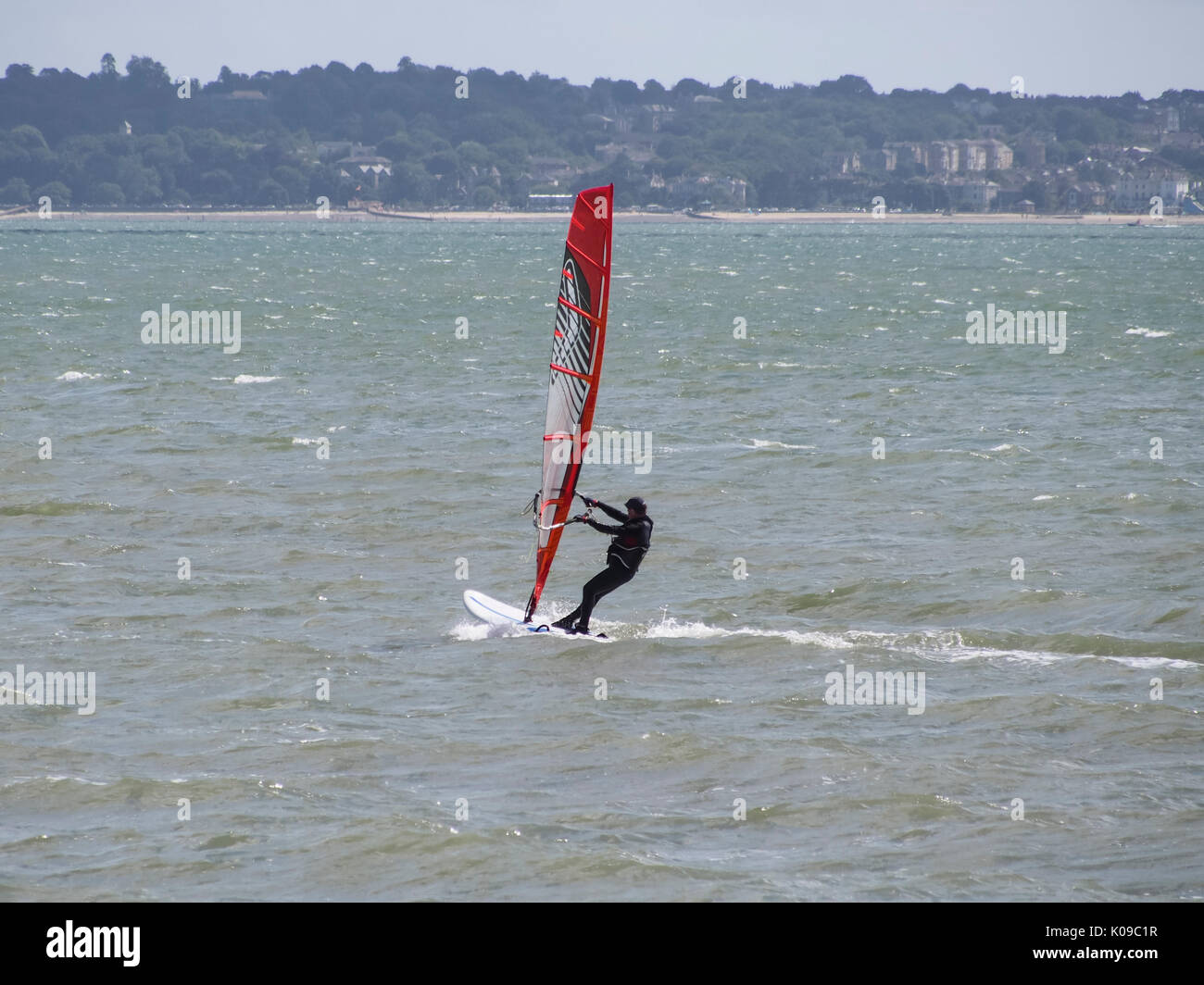 A wind surfer sails on the solent with the Isle of Wight in the ...