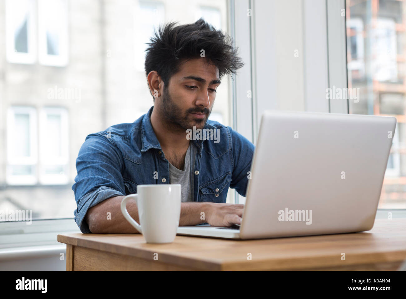 Portrait of an Indian man sitting at a table at home working on a ...