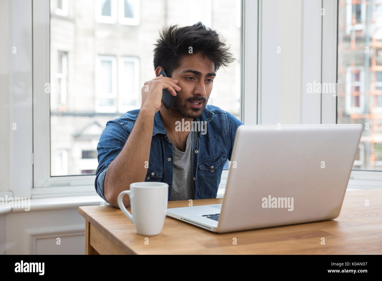 Portrait of an Indian man sitting at a table at home working on a ...