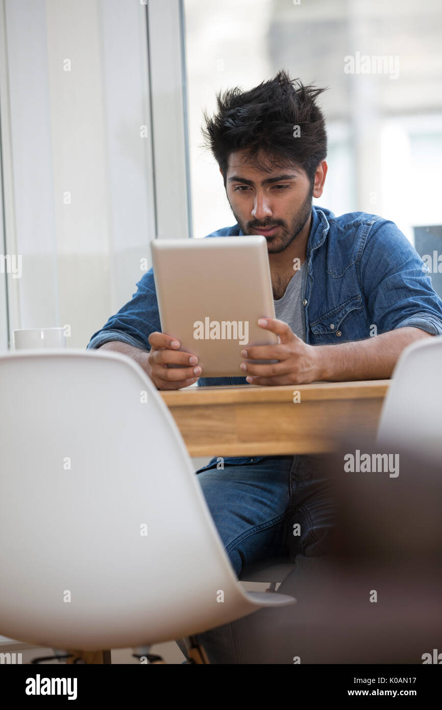 Portrait of an Indian man sitting at a table at home reading a Tablet ...