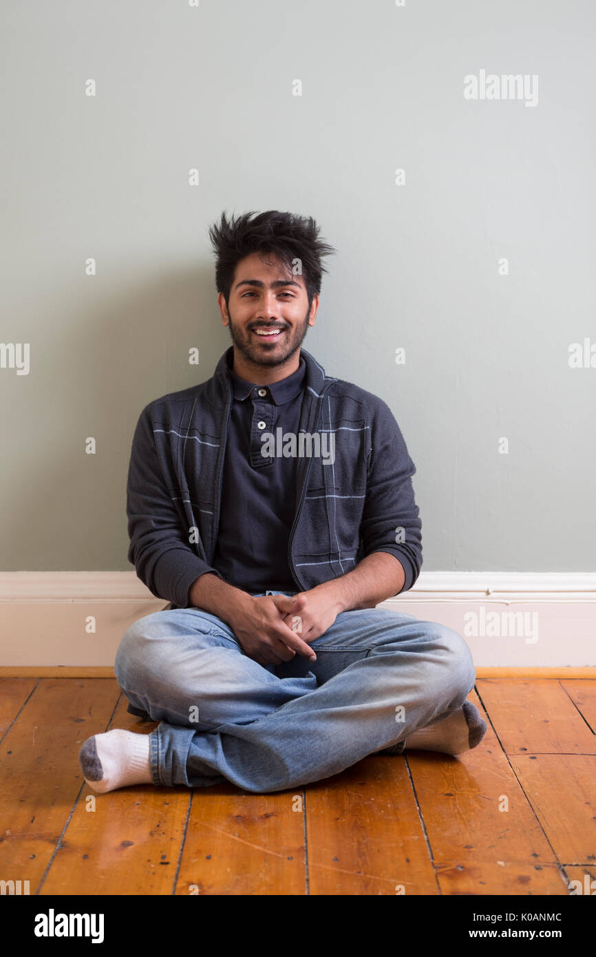 Portrait of a happy Indian man sitting on floor against green wall ...